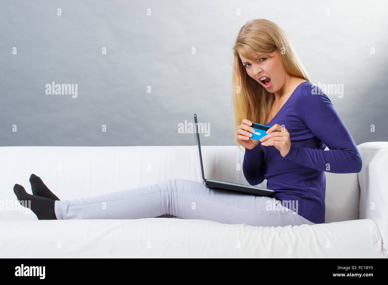 Angry woman using laptop sitting on sofa and breaking credit card ...