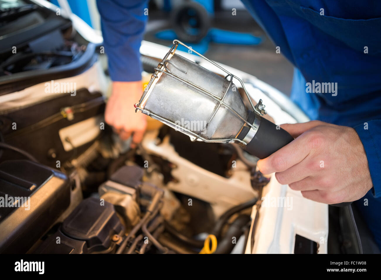 Mechanic examining under hood of car with torch Stock Photo - Alamy