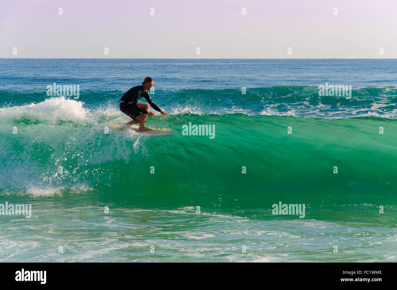 A surfer rides the nose of his board in crystal clear morning surf on ...