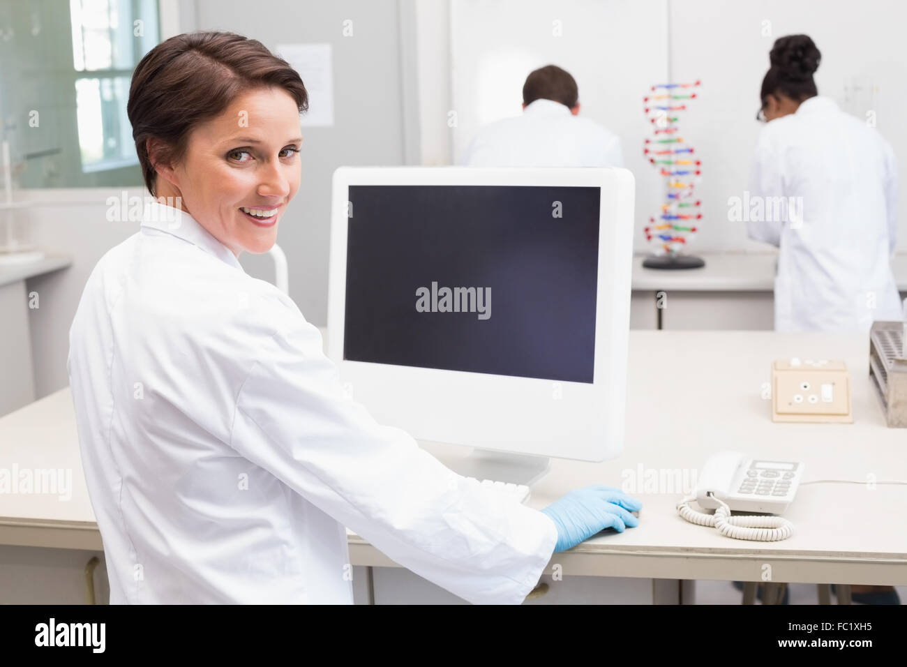 Smiling scientist using computer while colleagues working Stock Photo ...
