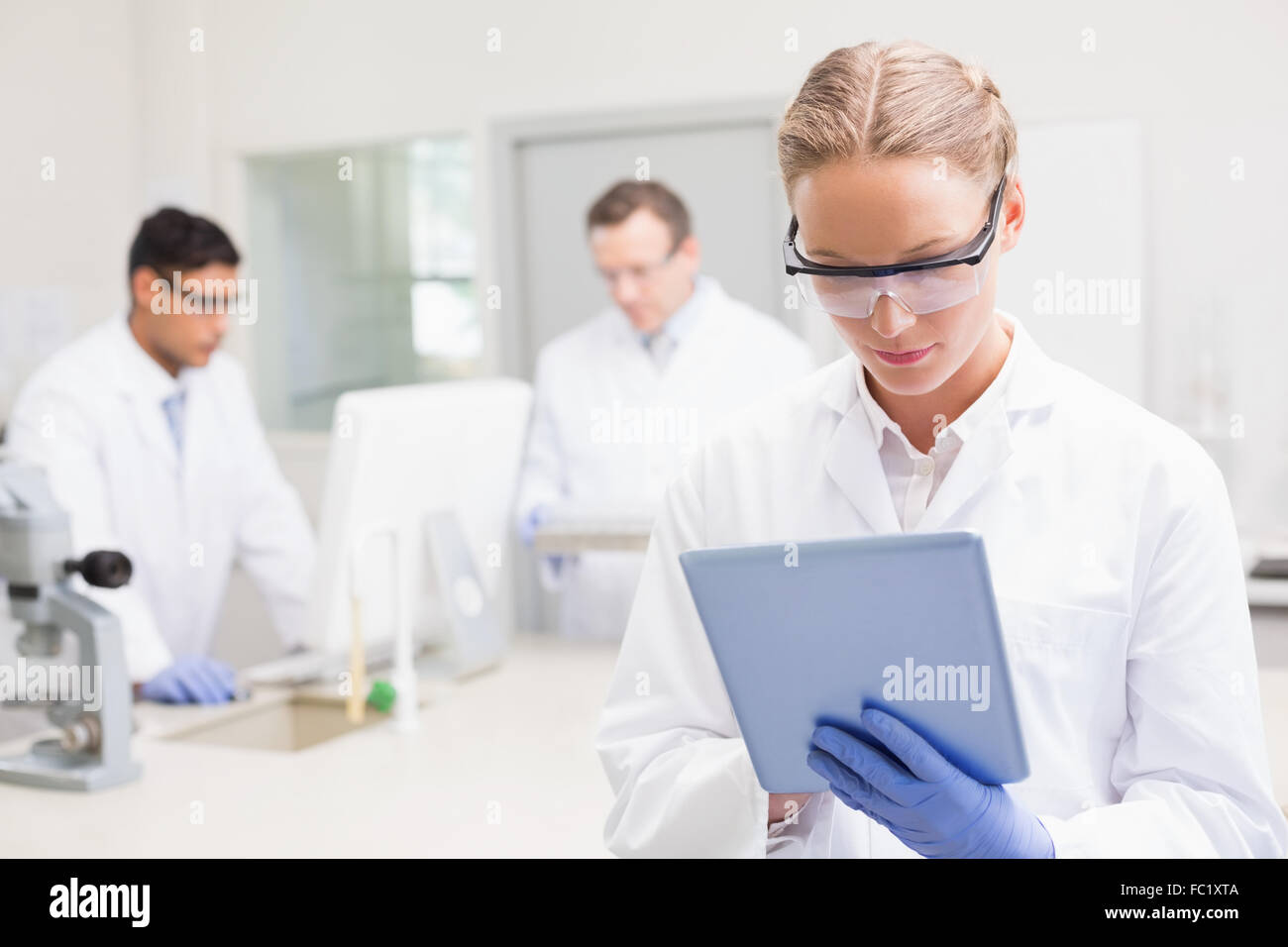 Scientist using tablet while colleagues working behind Stock Photo - Alamy