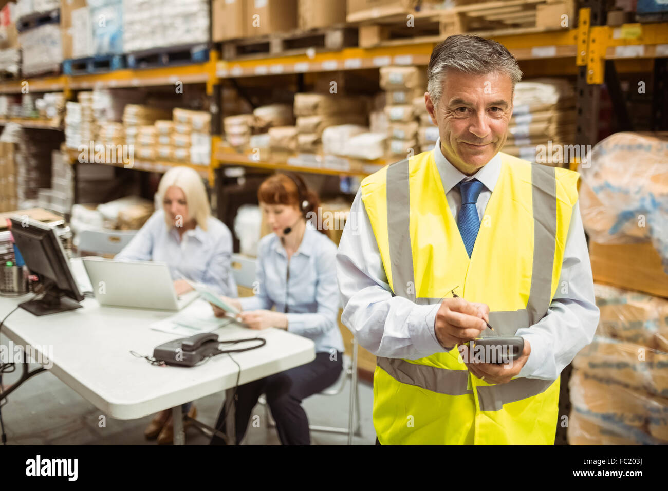 Smiling manager wearing yellow vest using handheld Stock Photo - Alamy