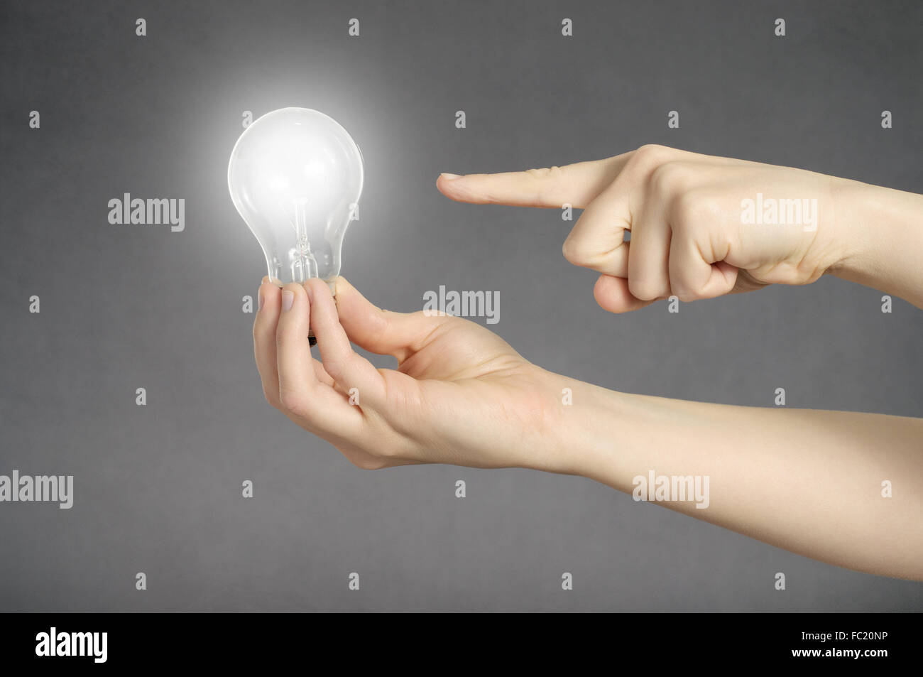 A finger pointing to a glowing light bulb in a hand Stock Photo - Alamy