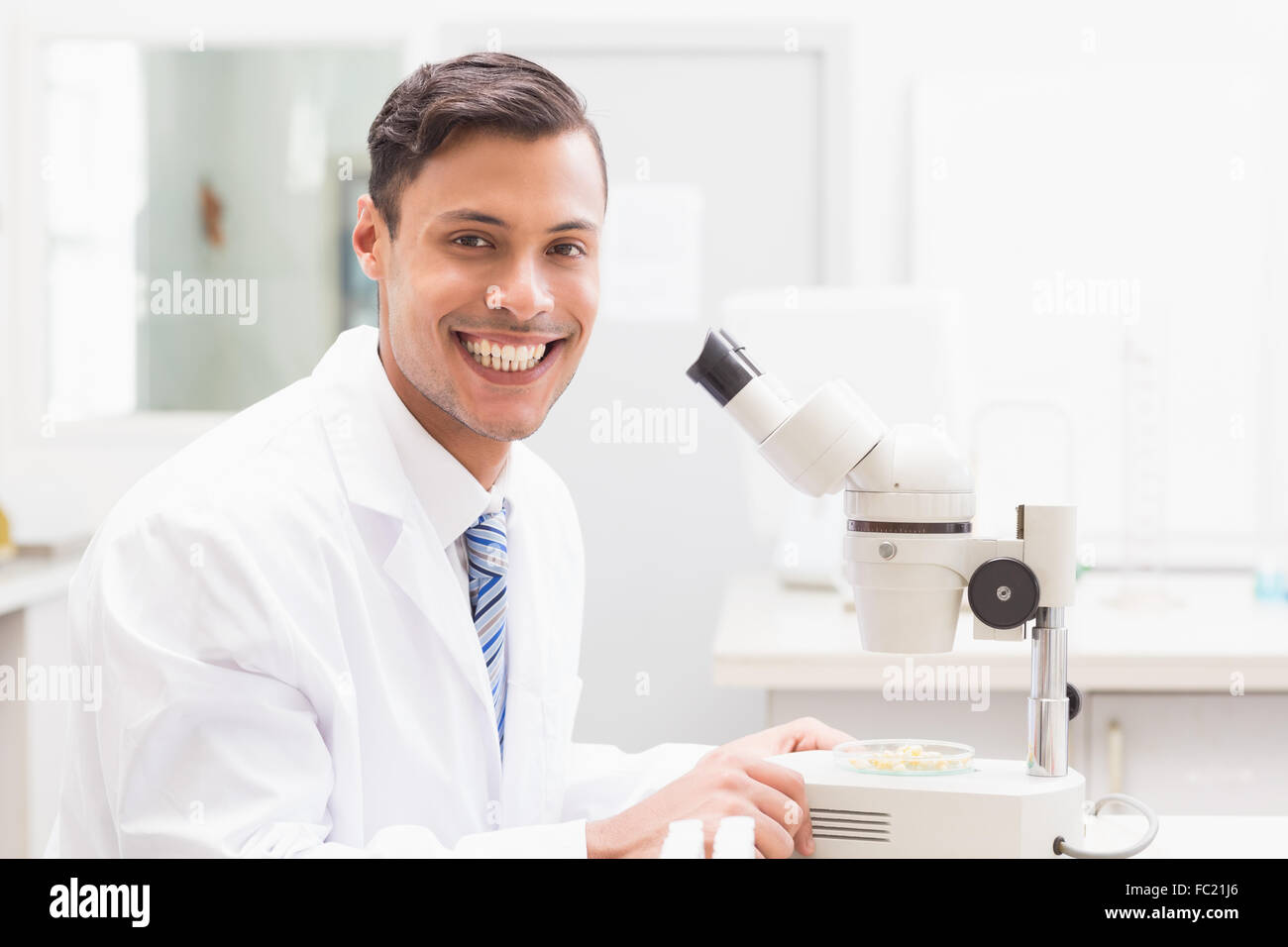 Smiling scientist observing petri dish with microscope Stock Photo - Alamy