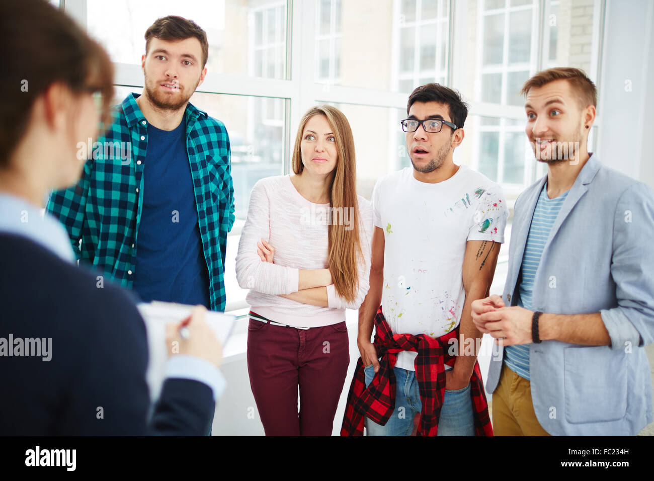Group of astonished young people looking at their friend at ...