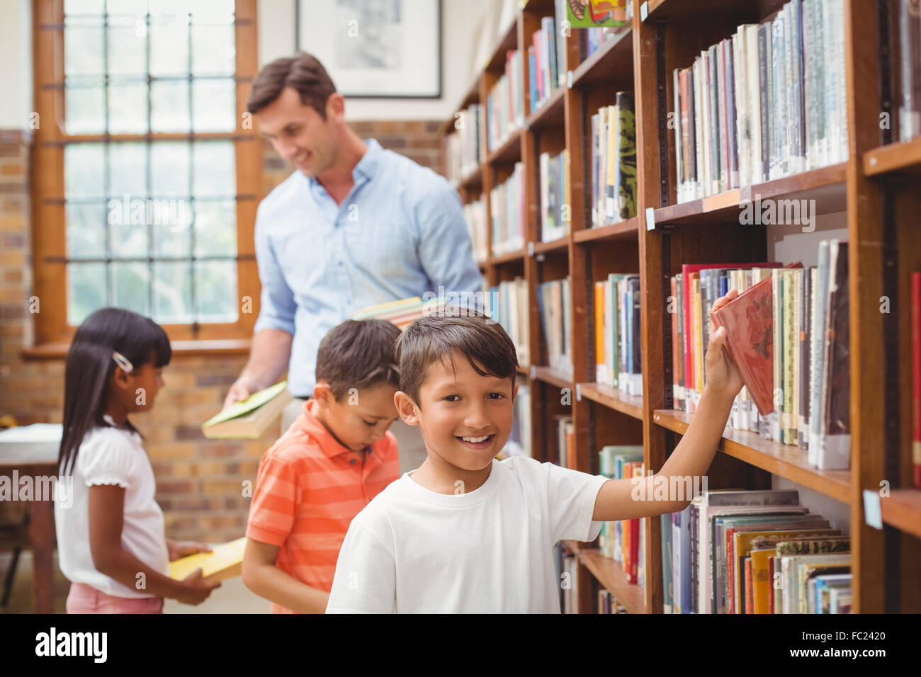 Cute pupils and teacher looking for books in library Stock Photo - Alamy
