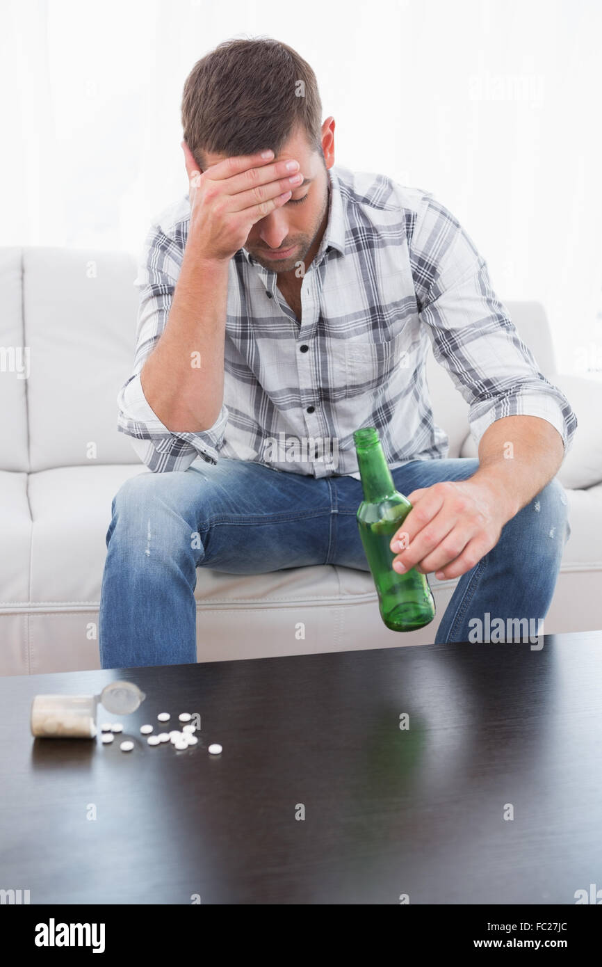 Hungover man with a beer and his medicine laid out on coffee table ...