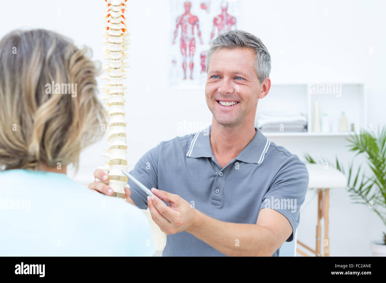 Smiling physiotherapist showing spine model to his patient Stock Photo ...