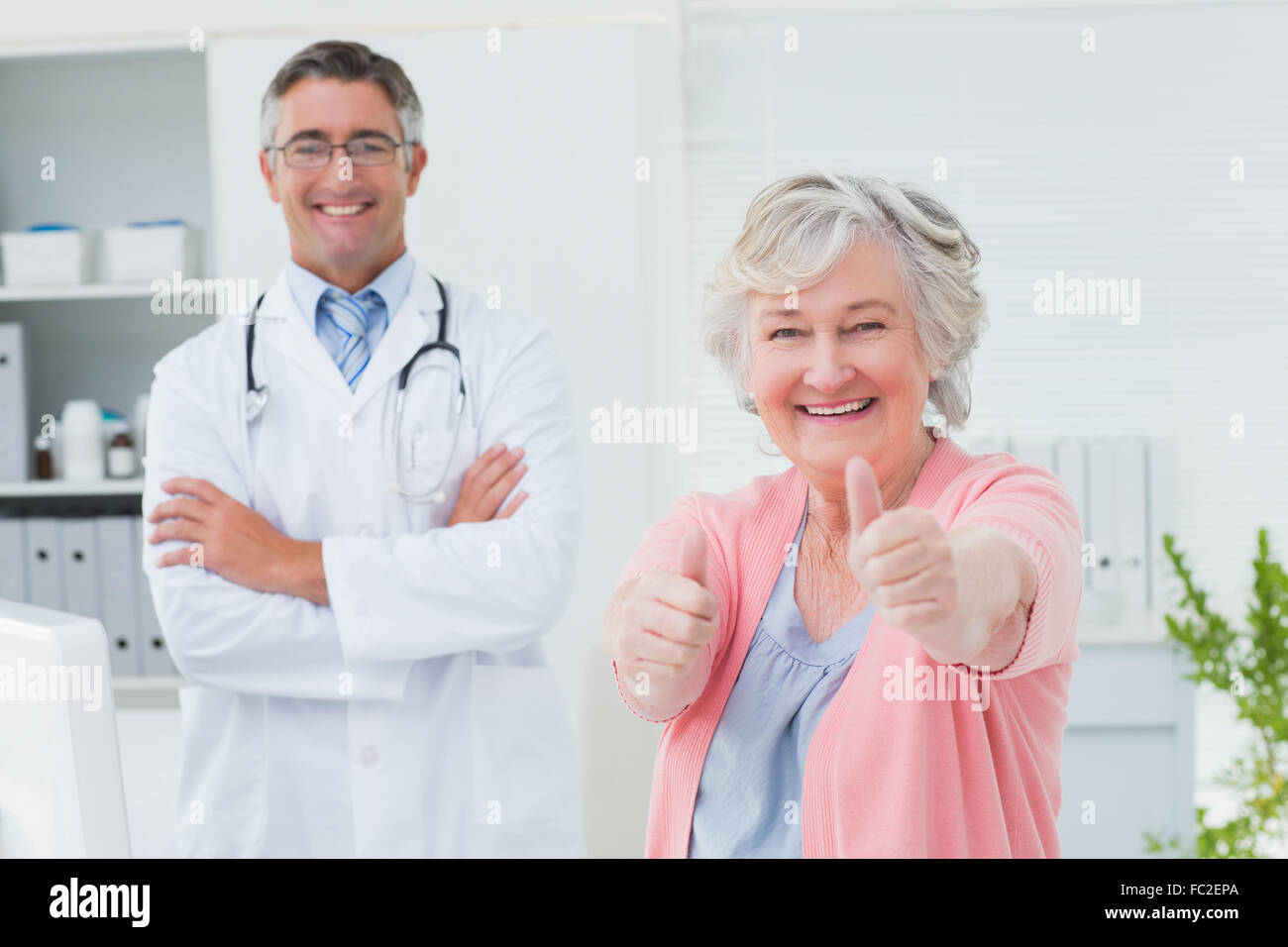 Patient showing thumbs up sign while standing with doctor Stock Photo ...