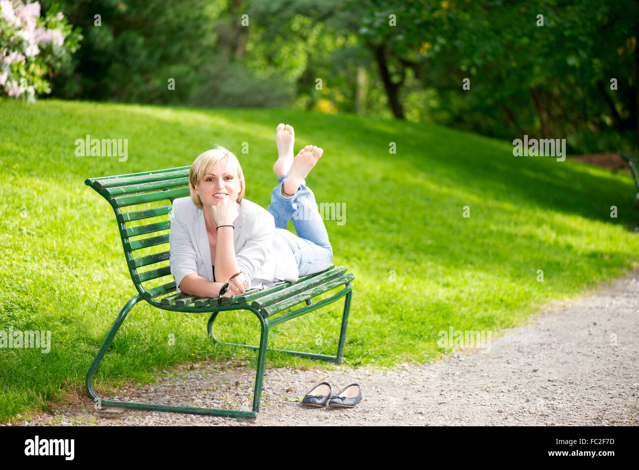 Young woman laying on bench in park Stock Photo - Alamy