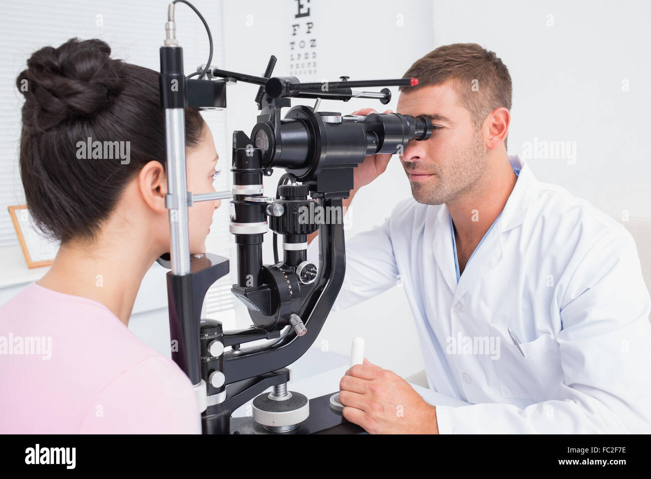 Optician examining female patients eyes through slit lamp Stock Photo - Alamy