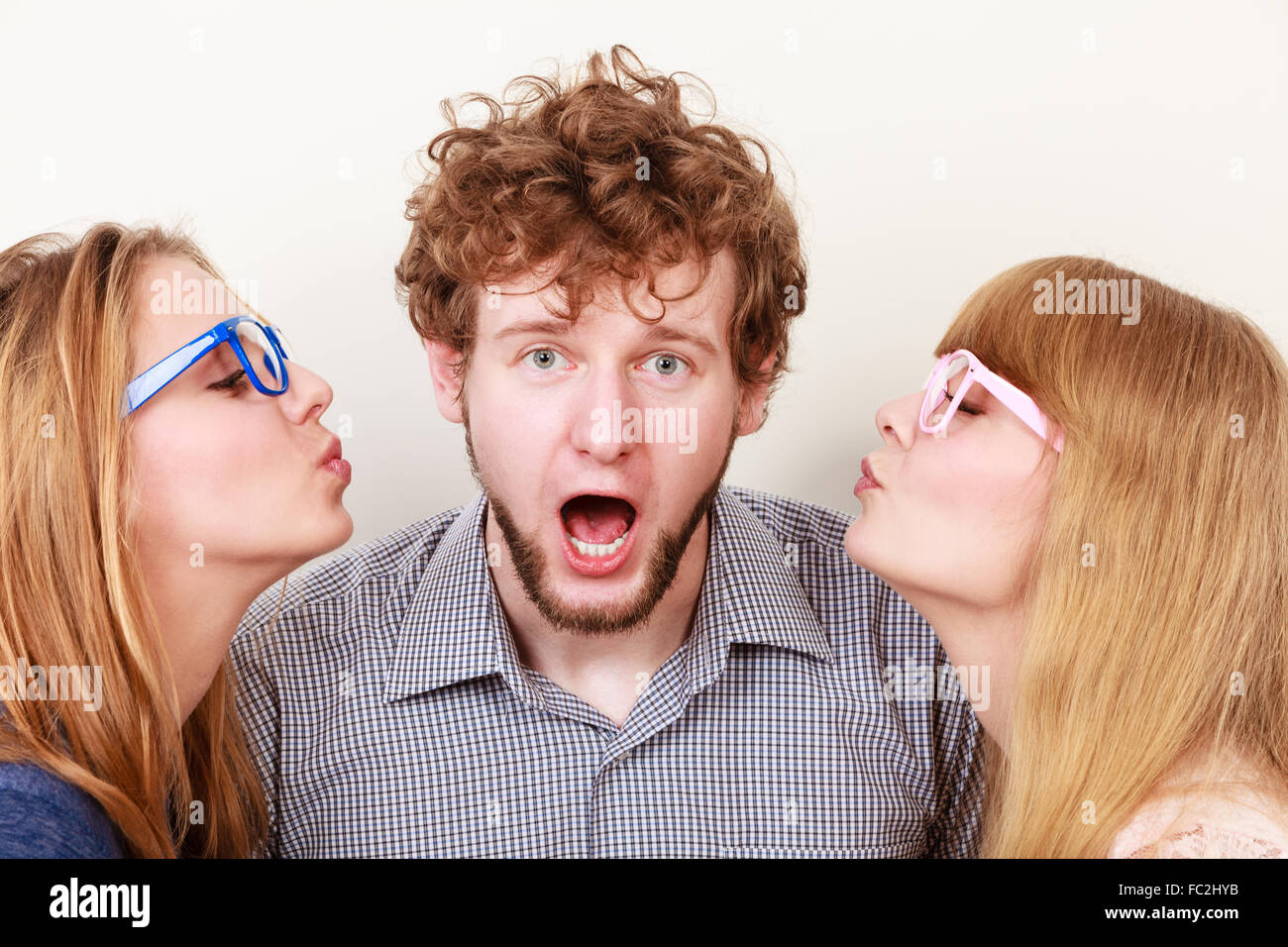 Two pretty young women in glasses kissing handsome man. Love triangle ...