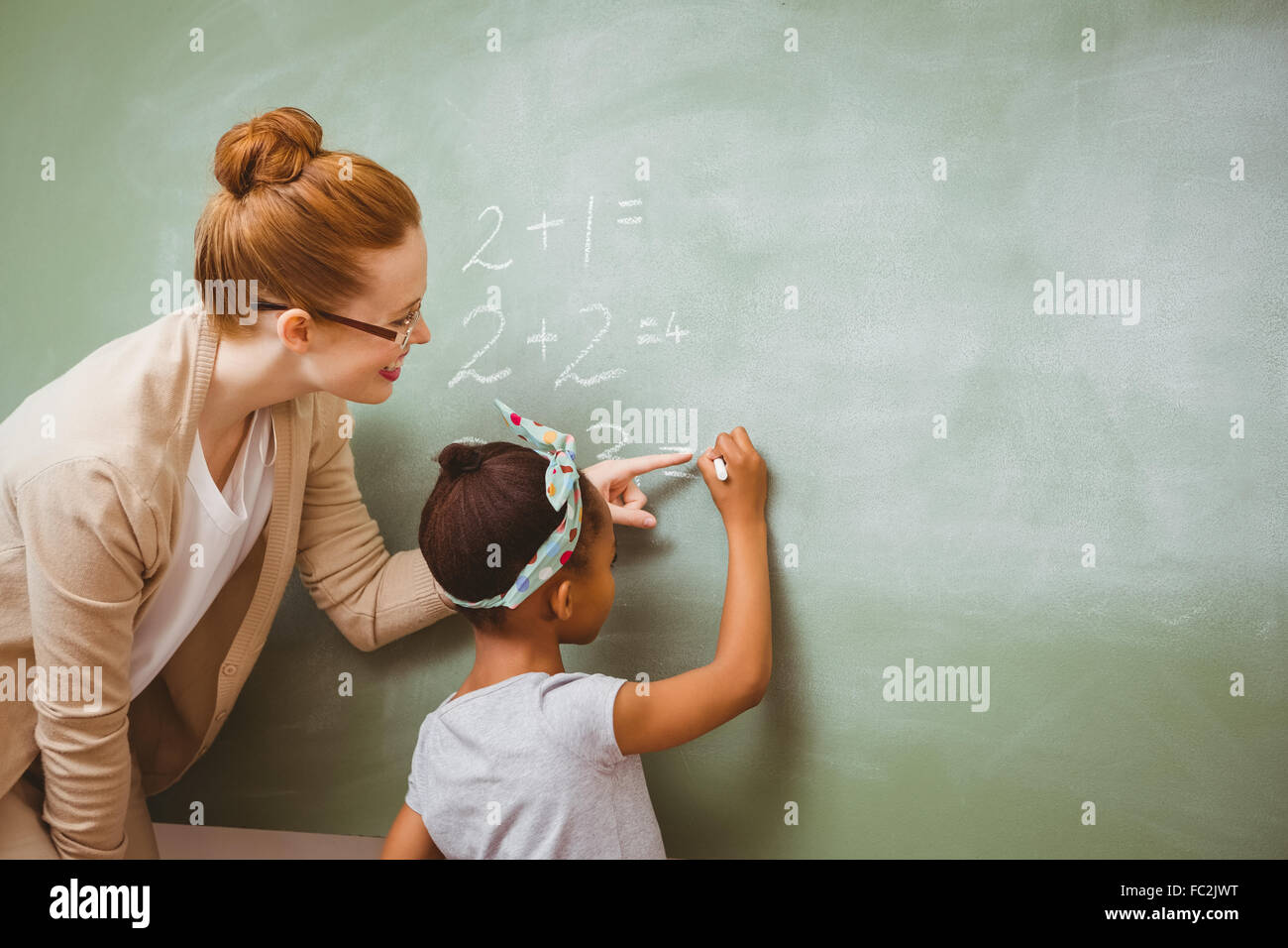 Teacher assisting girl to write on blackboard in classroom Stock Photo ...