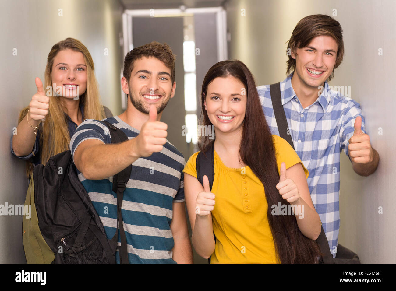 Happy students gesturing thumbs up at college corridor Stock Photo - Alamy