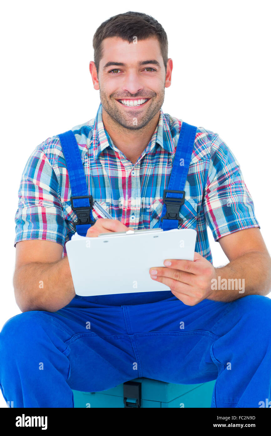 Happy plumber writing on clipboard while sitting on toolbox Stock Photo ...