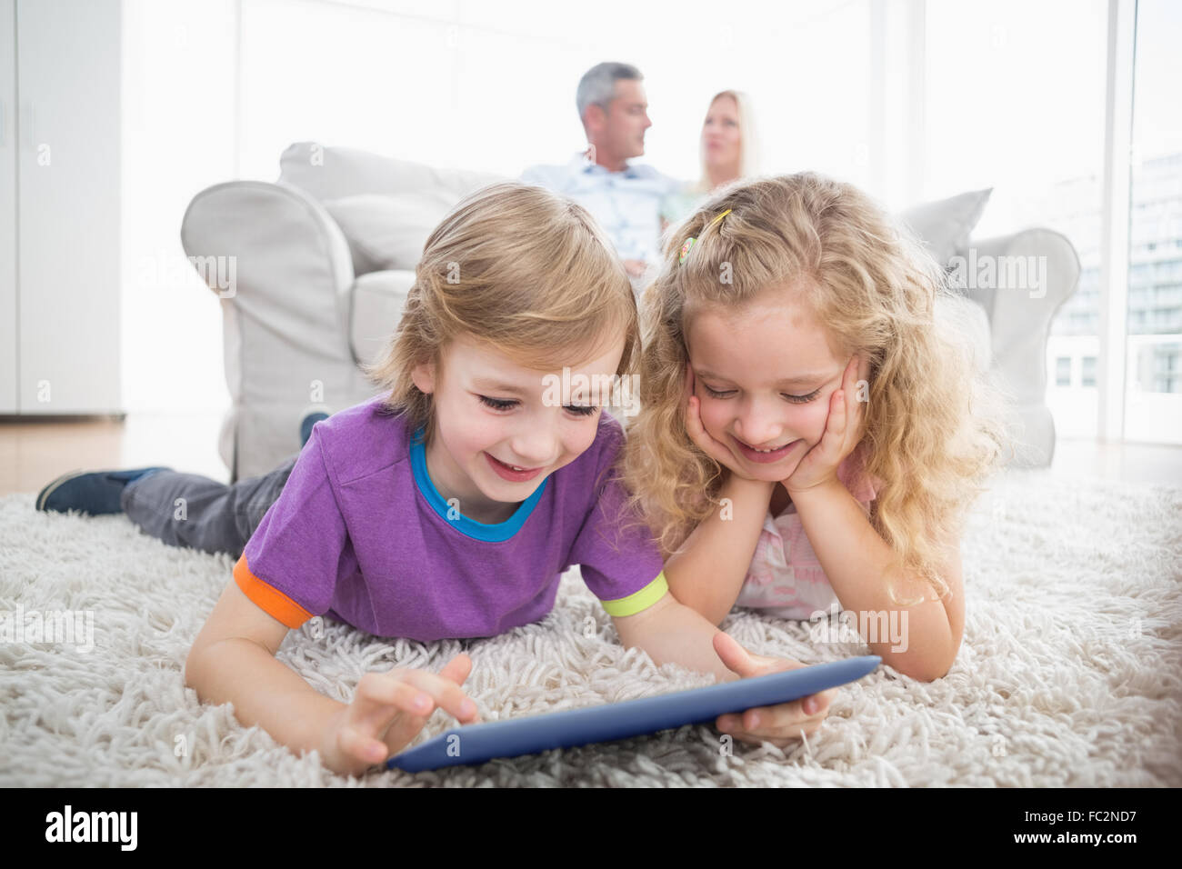 Siblings using digital tablet on rug at home Stock Photo - Alamy
