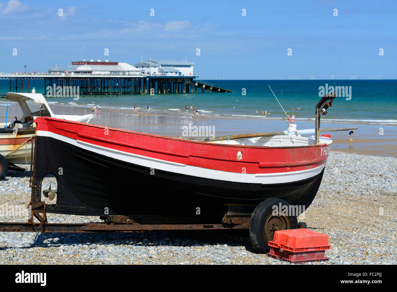 Red and black colored fishing boat on beach in front of Cromer pier ...