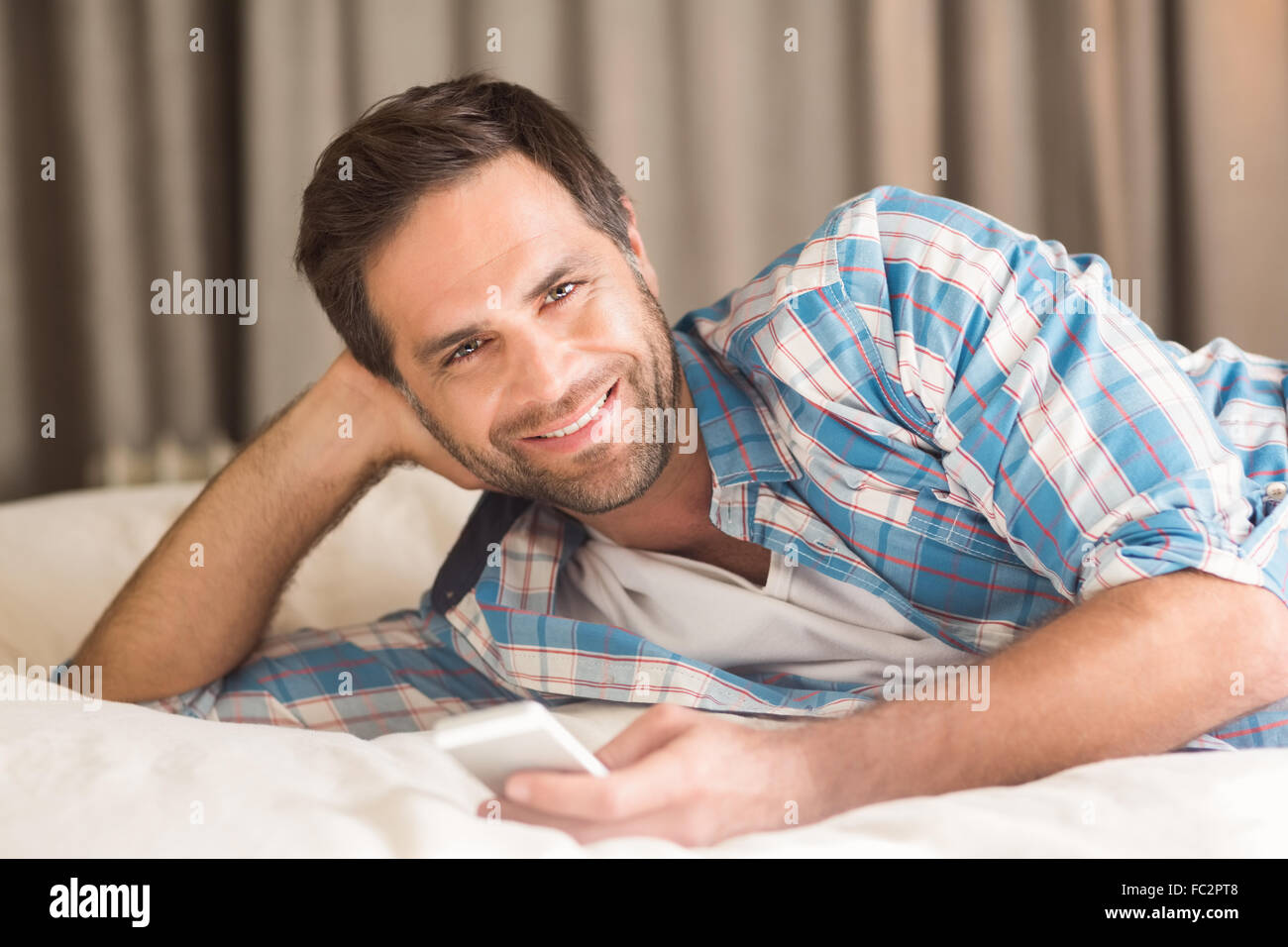 Handsome man relaxing on his bed using his phone Stock Photo - Alamy