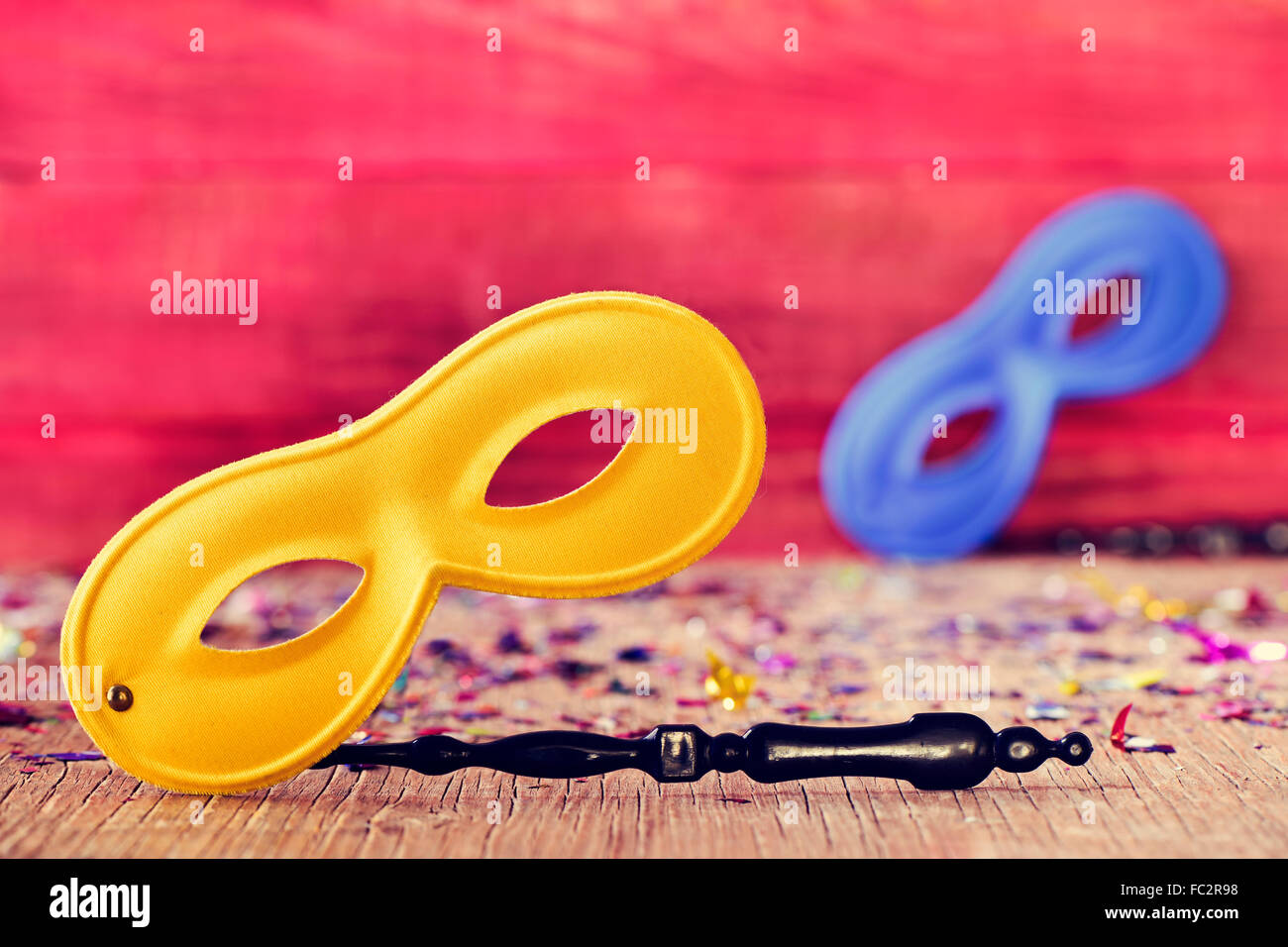 two handled carnival masks, one yellow and one blue, and confetti of ...