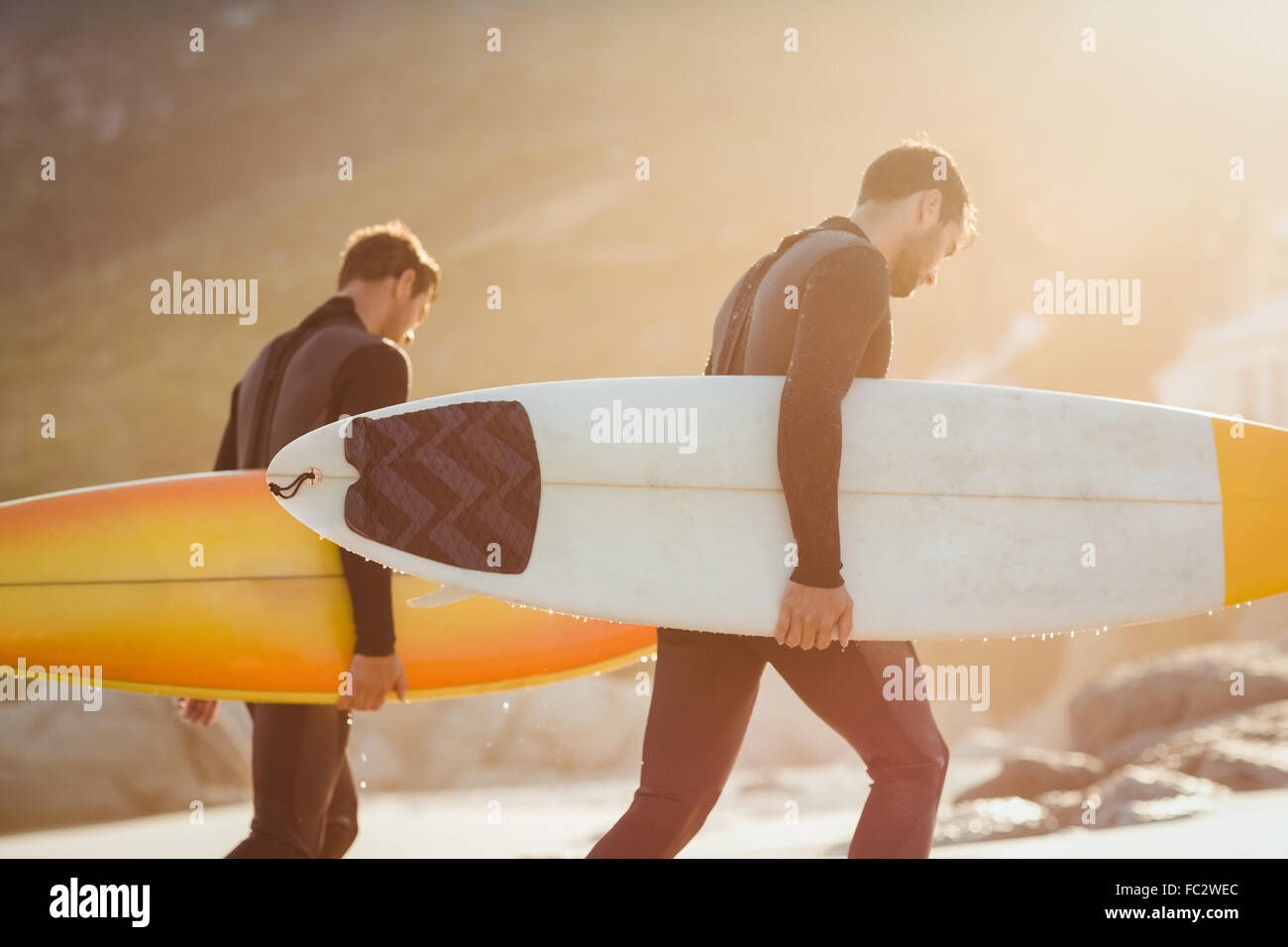 Two men in wetsuits with a surfboard on a sunny day Stock Photo - Alamy