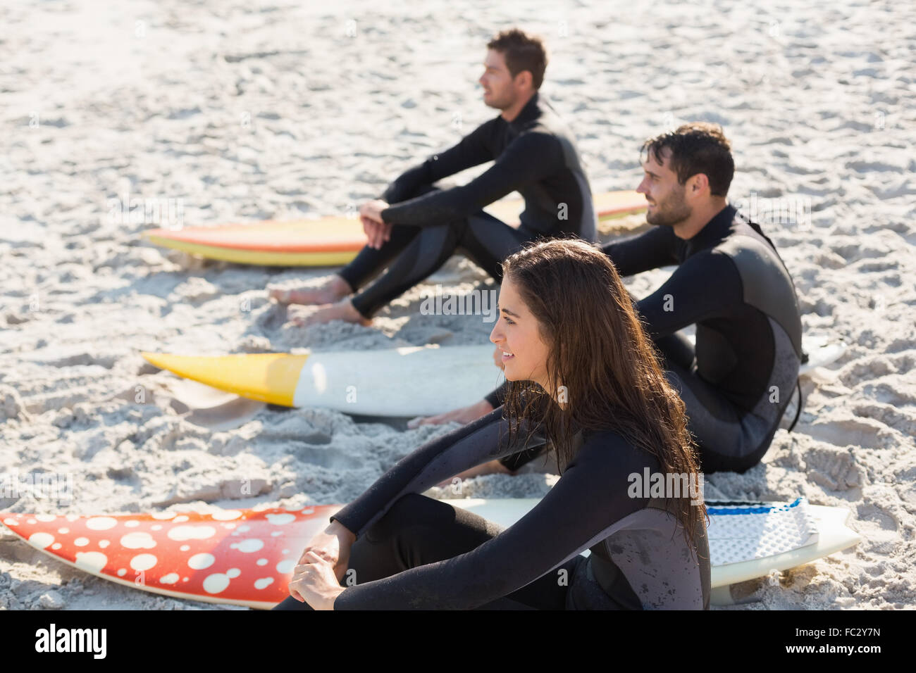Group of friends on wetsuits with a surfboard on a sunny day Stock ...