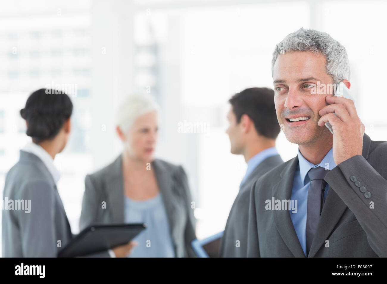 Businessman using a smartphone with colleagues behind Stock Photo - Alamy