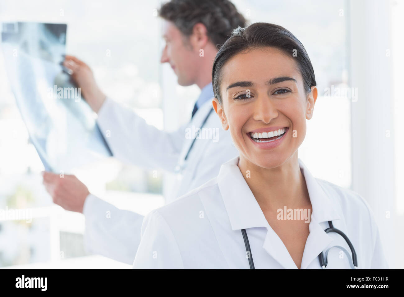 Female doctor smiling at camera while her colleague looking at X-ray ...