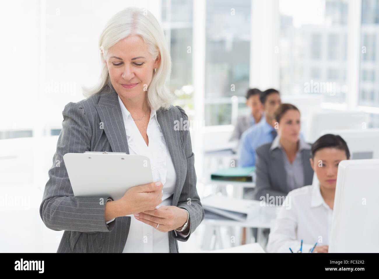 Businesswoman checking her clipboard while team work using computer ...
