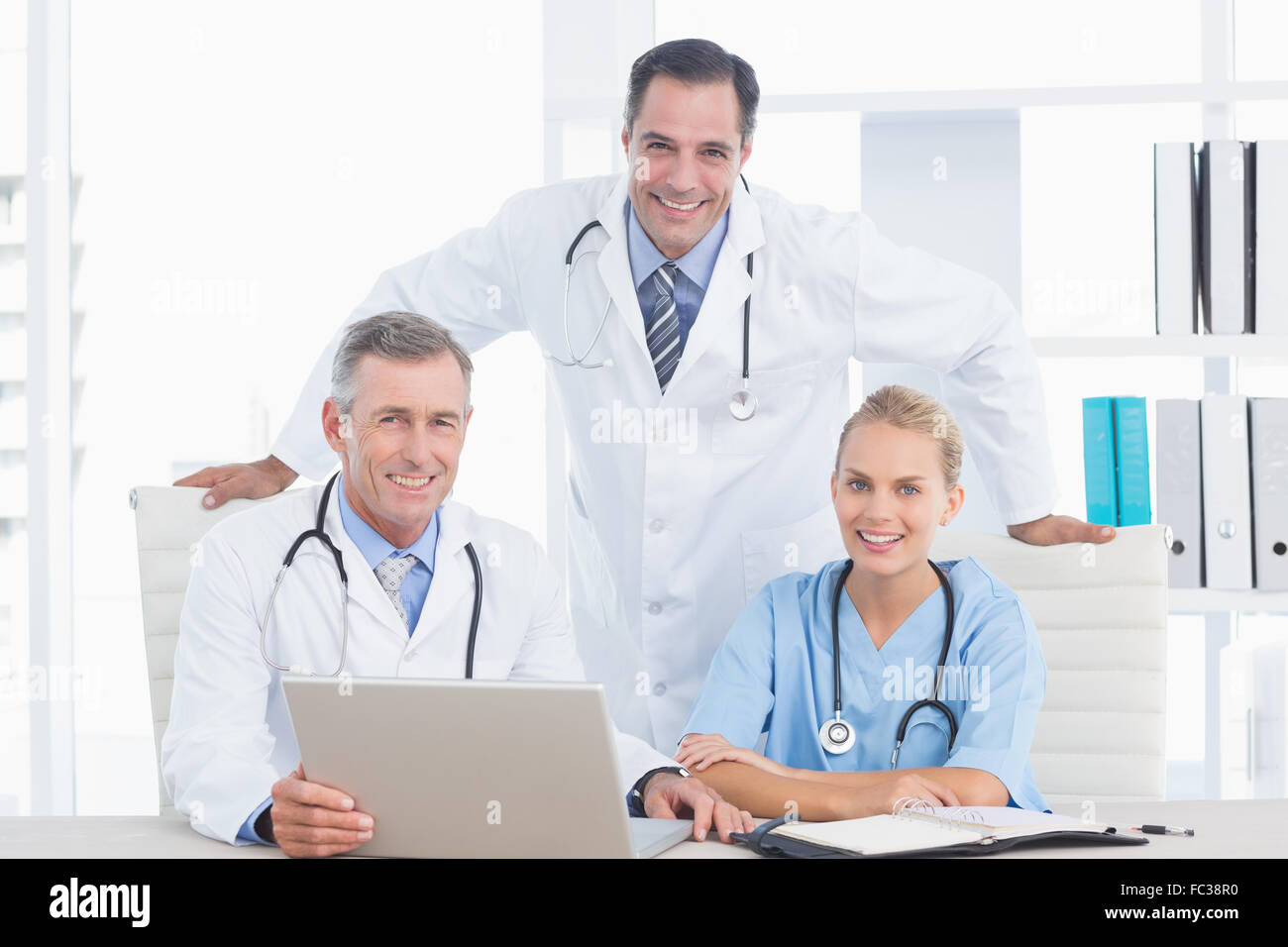 Smiling doctors and nurse looking at camera in front of laptop Stock ...