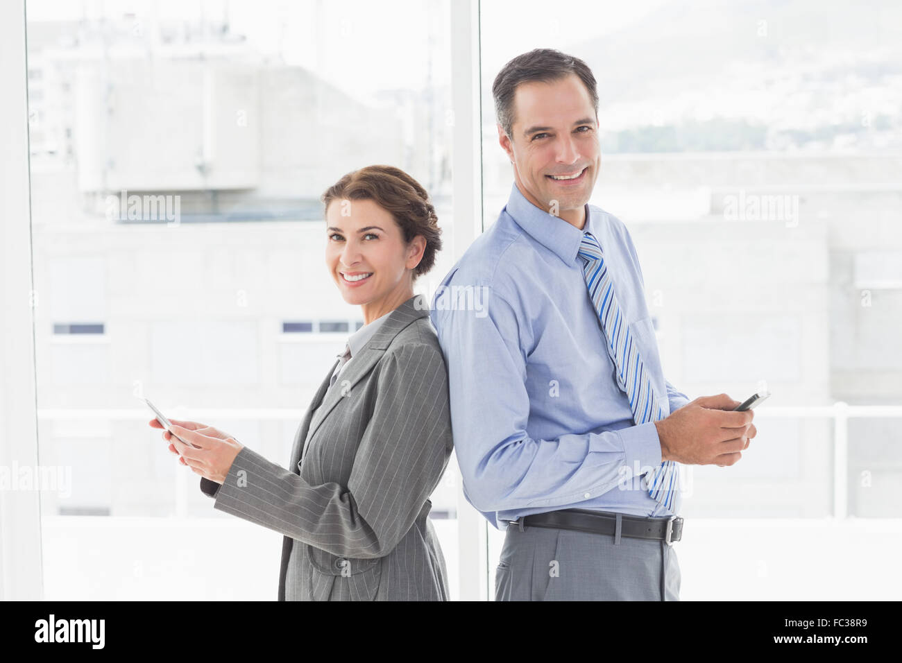 Smiling businesswoman back-to-back with colleague Stock Photo - Alamy