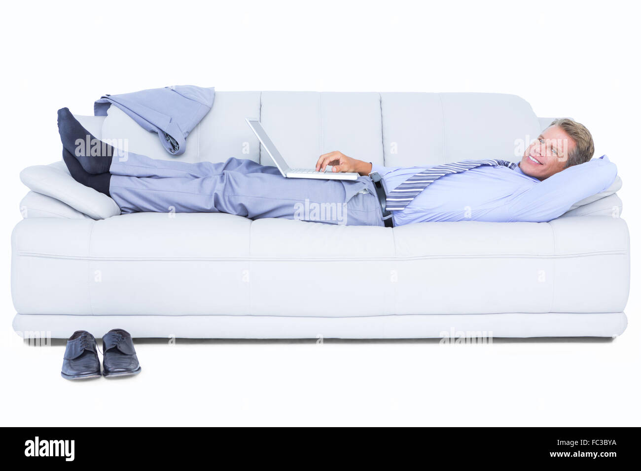 Businessman lying on sofa using his laptop smiling at camera Stock ...