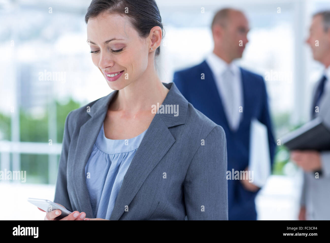 businesswoman using her phone with two colleague behind her Stock Photo ...