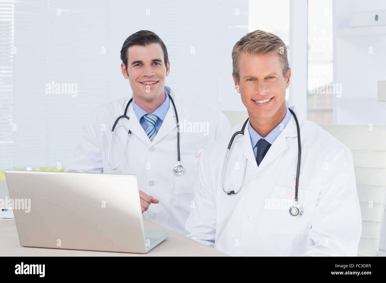 Smiling doctors looking at camera in front of laptop Stock Photo - Alamy