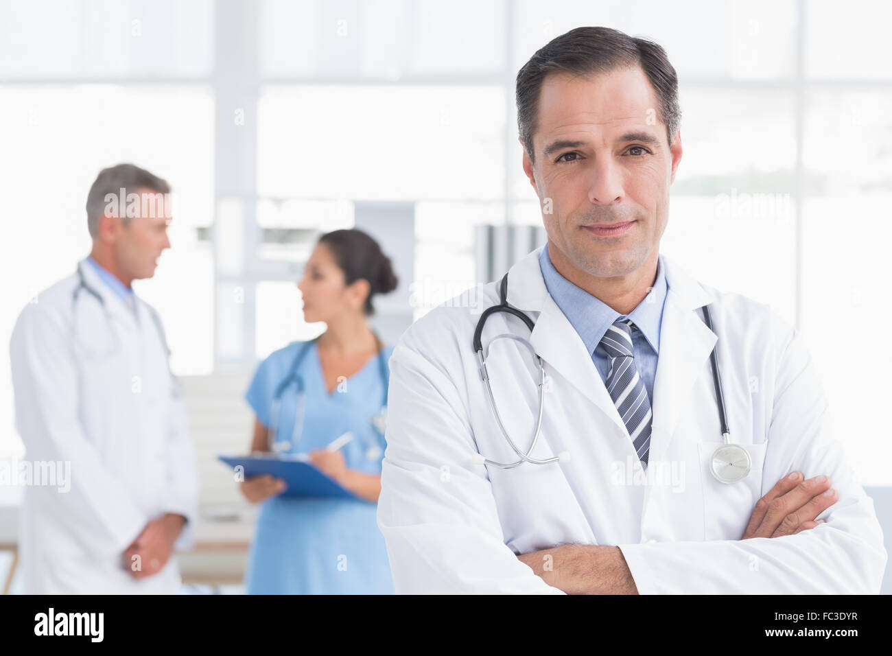 Doctor looking at camera while his colleagues works Stock Photo - Alamy