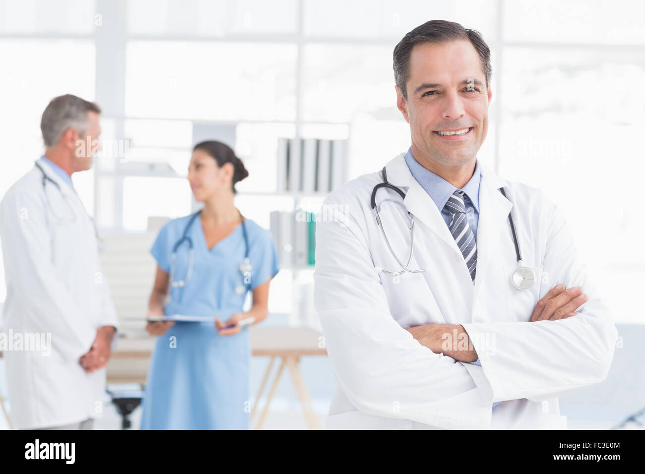 Doctor looking at camera while his colleagues works Stock Photo - Alamy