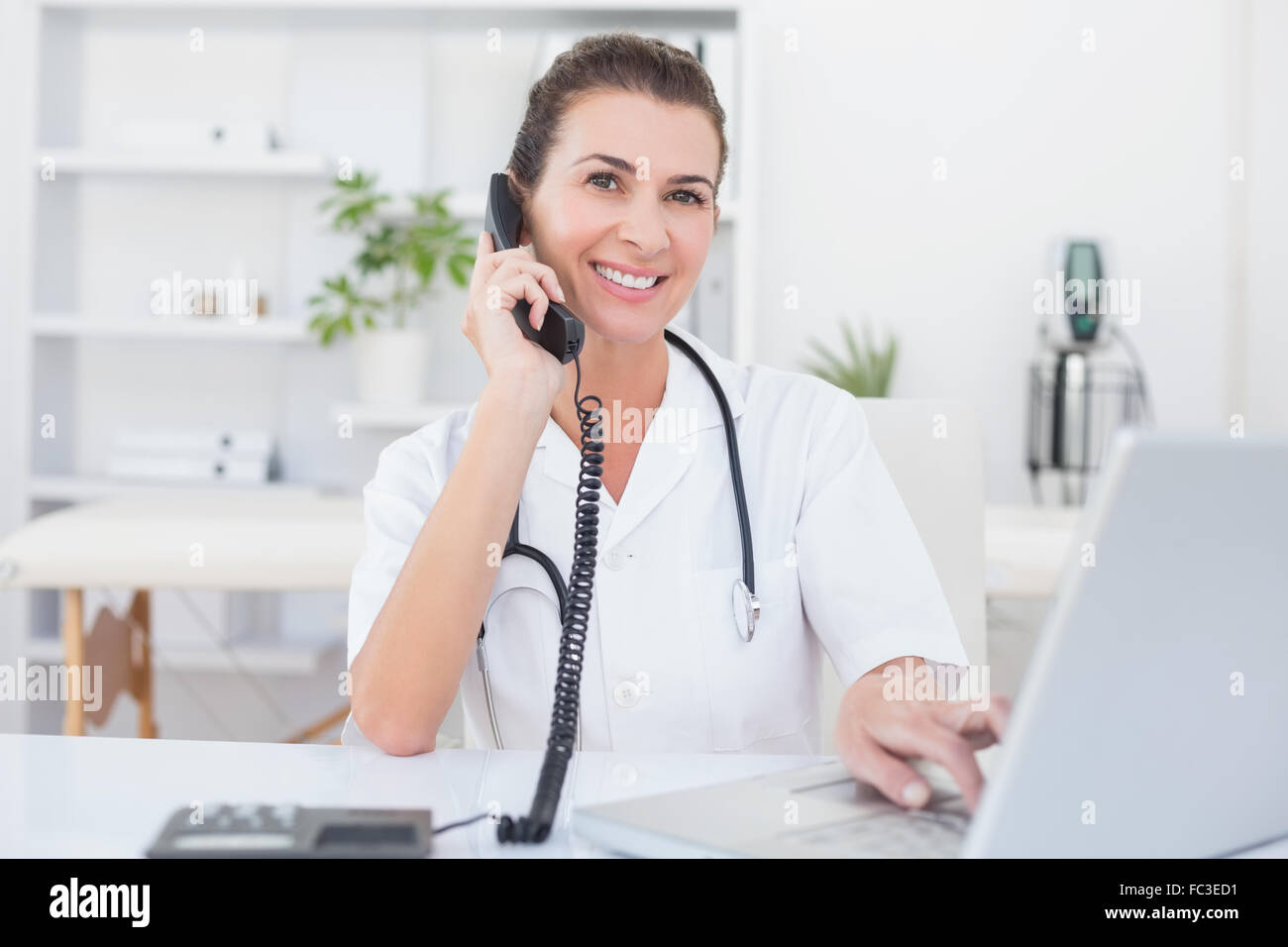 Doctor doing phone call while she using computer Stock Photo - Alamy