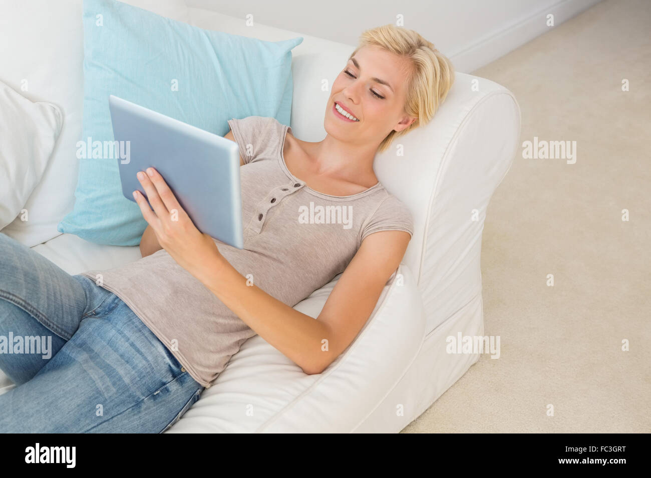 Smiling blonde woman using digital tablet on the sofa Stock Photo - Alamy