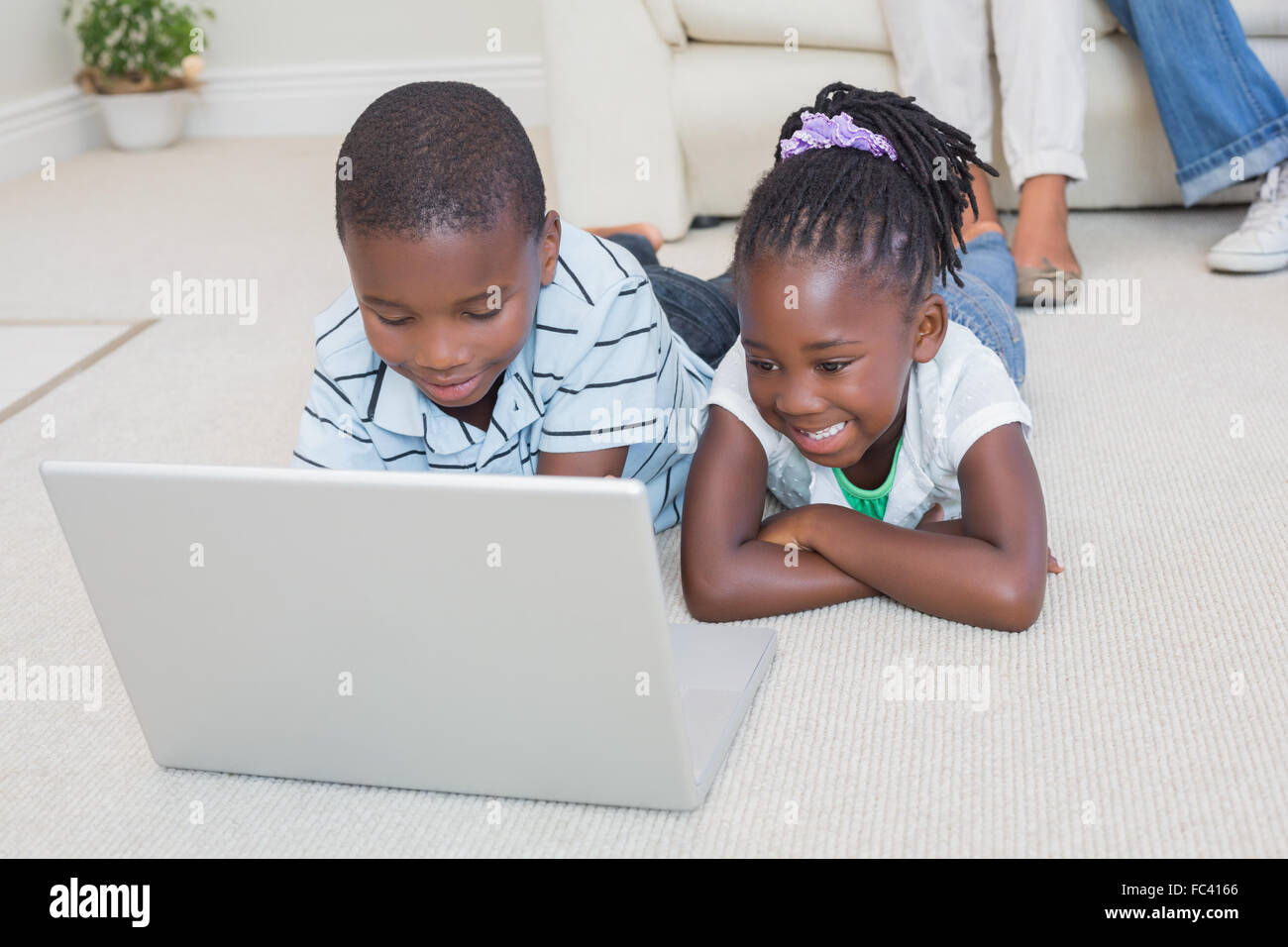 Happy siblings lying on the floor using laptop Stock Photo - Alamy