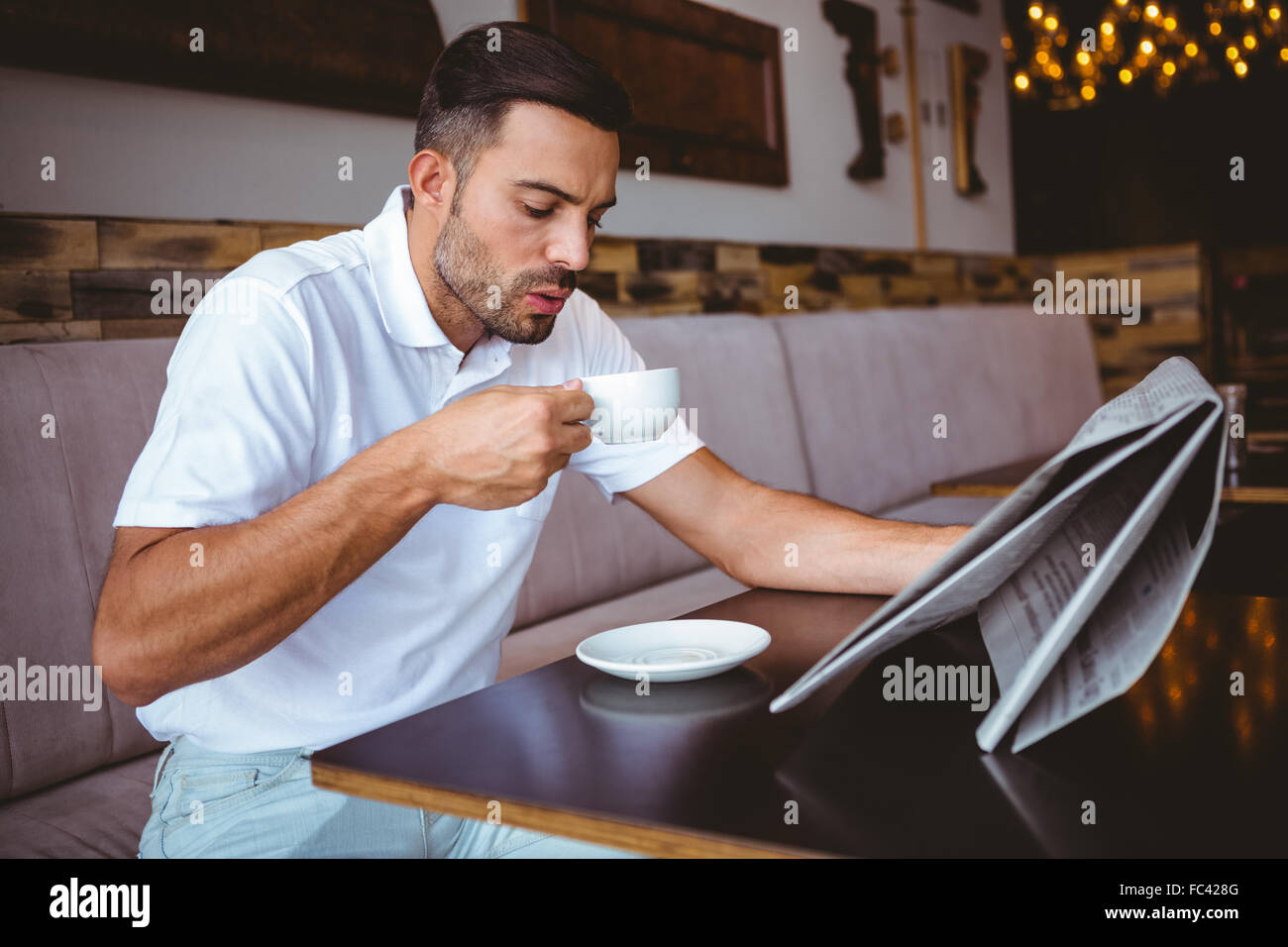 Young man drinking cup of coffee reading newspaper Stock Photo - Alamy