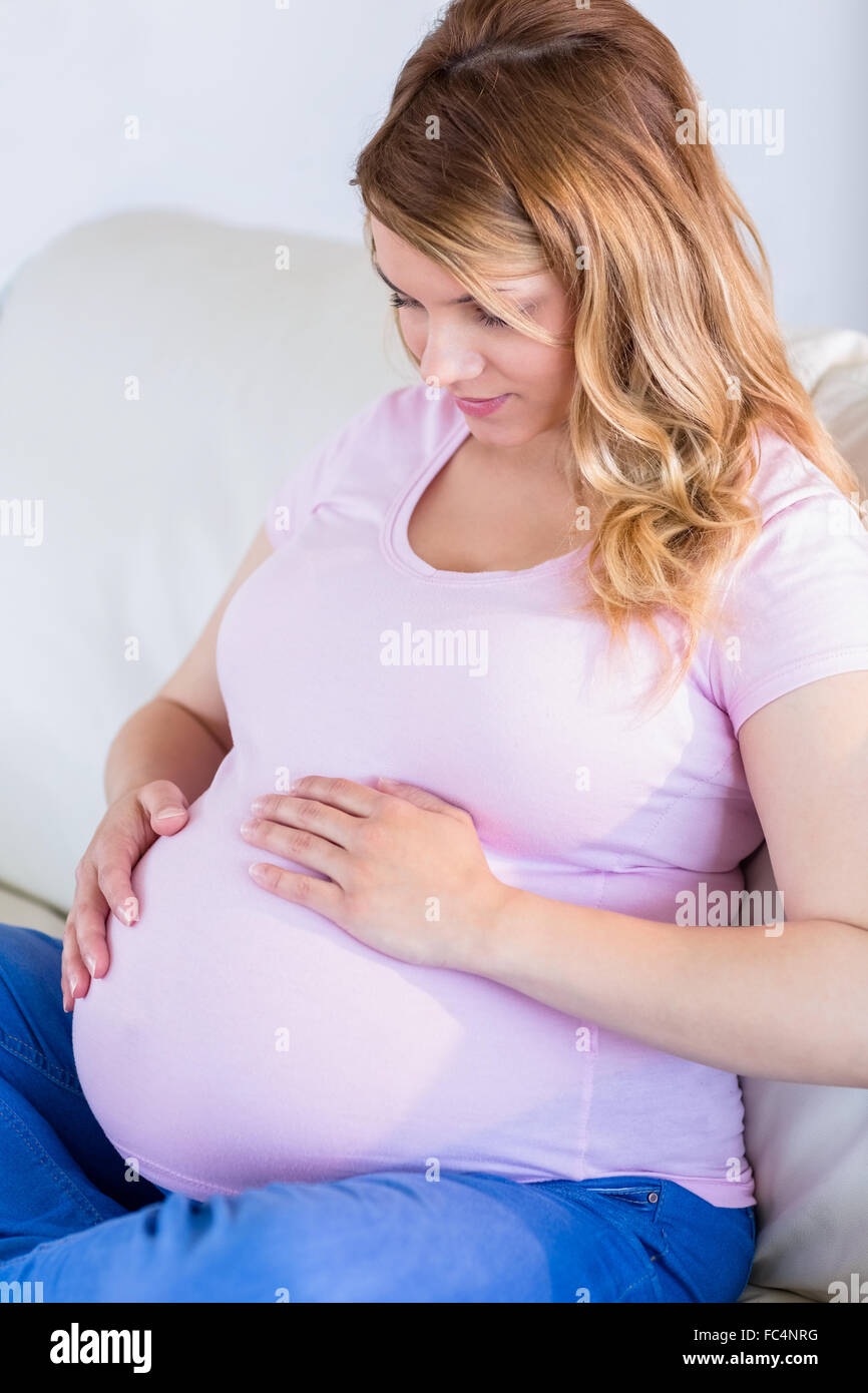 Pregnant woman sitting on couch touching her belly Stock Photo - Alamy