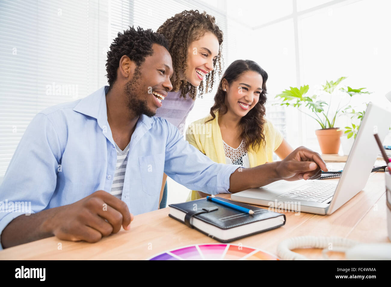 Happy coworkers using laptop and pointing the screen Stock Photo - Alamy