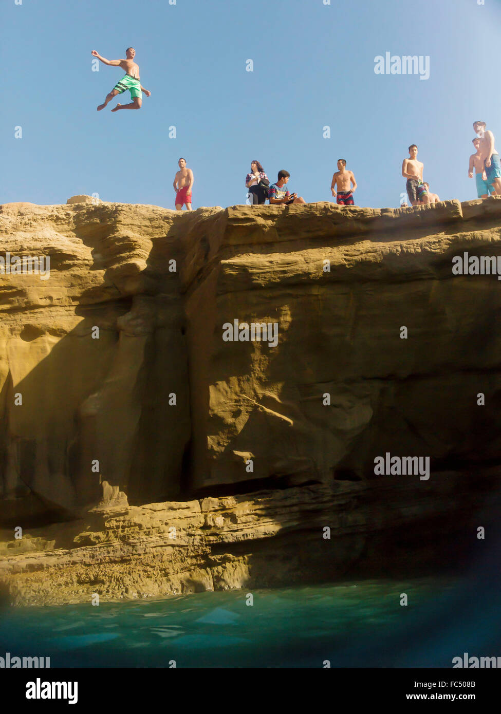 A cliff diver dives from cliff at San Diego, California during sunset ...