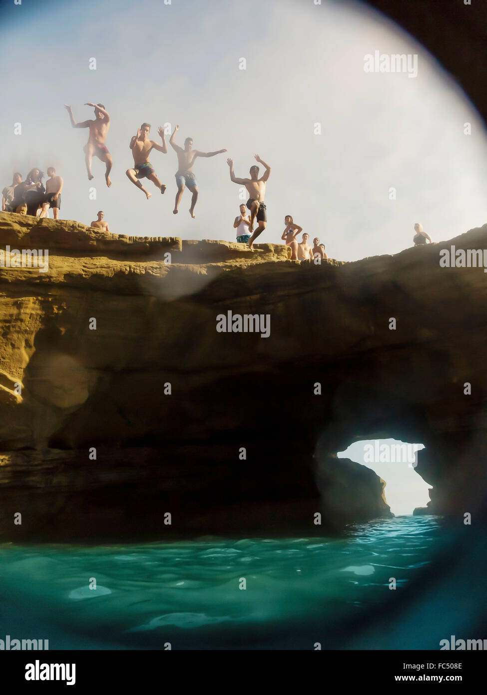 Four men dive from cliff at San Diego, California during sunset and few ...