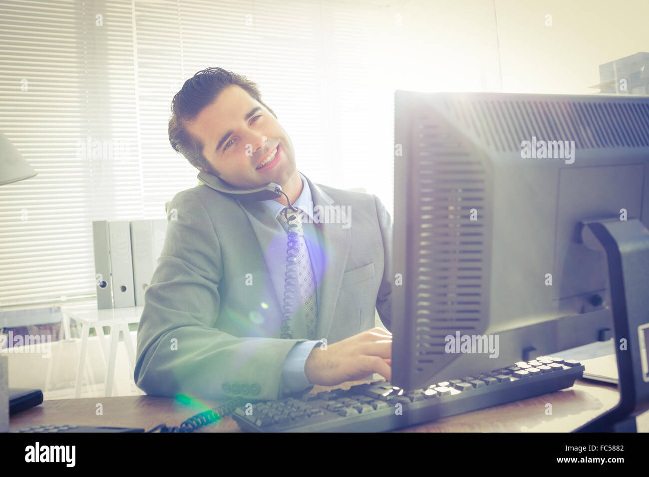 Businessman having phone call while using his computer Stock Photo - Alamy