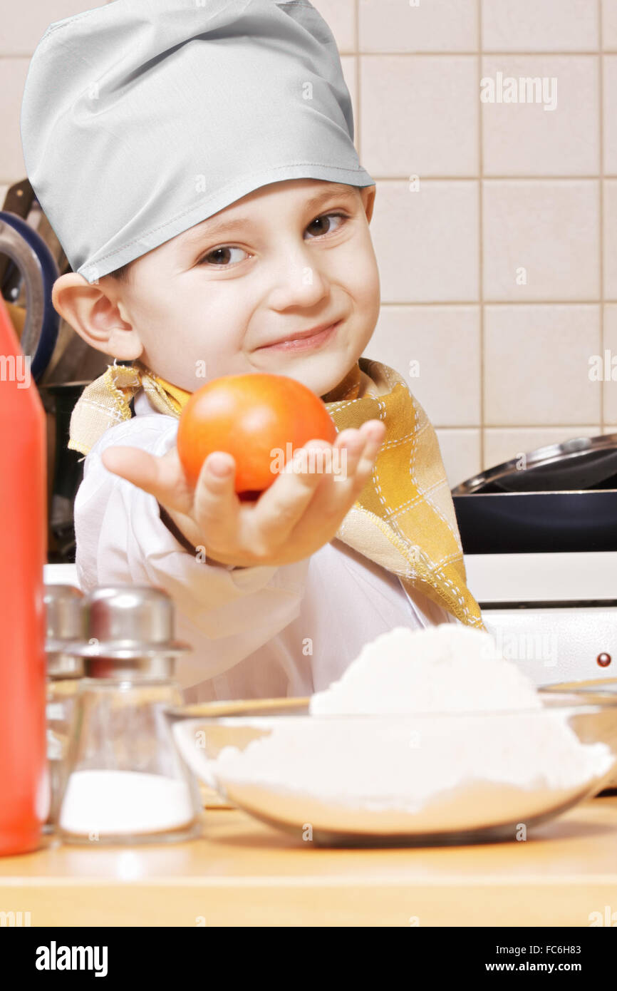 Cute little cook giving tomato Stock Photo - Alamy
