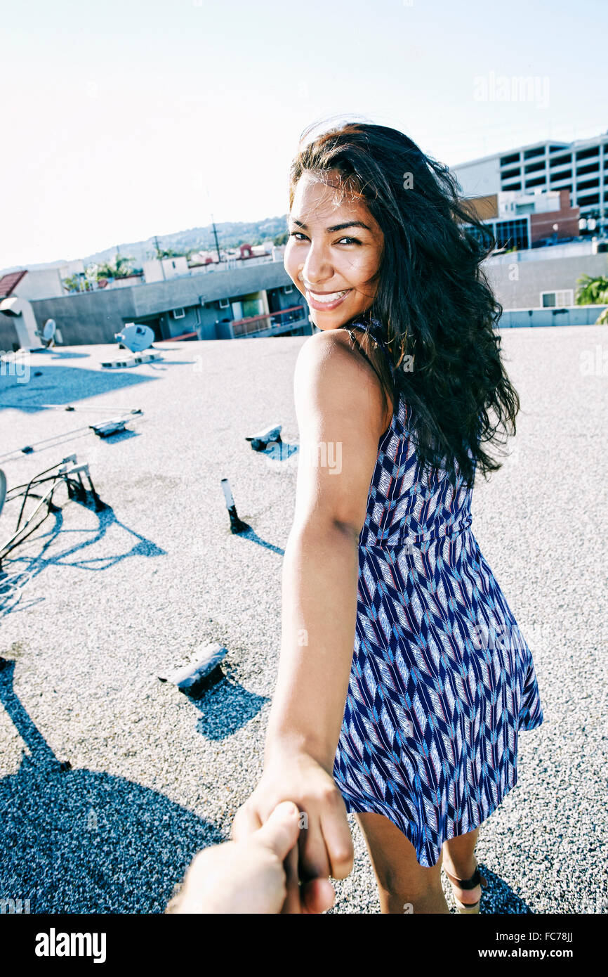 Hispanic woman pulling hand on urban rooftop Stock Photo - Alamy