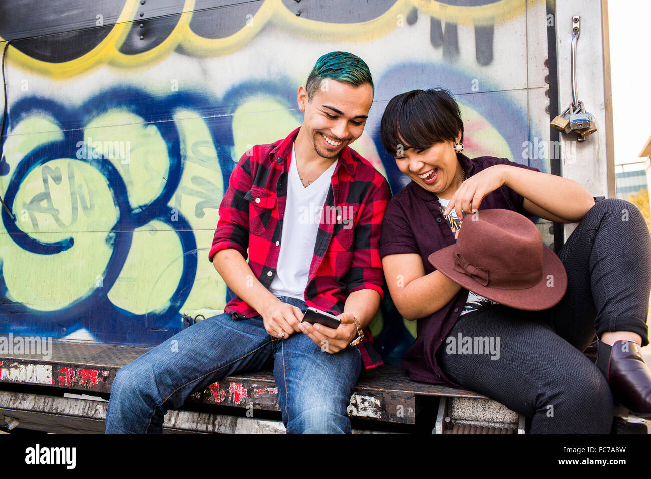 Friends using cell phone on graffiti truck Stock Photo - Alamy