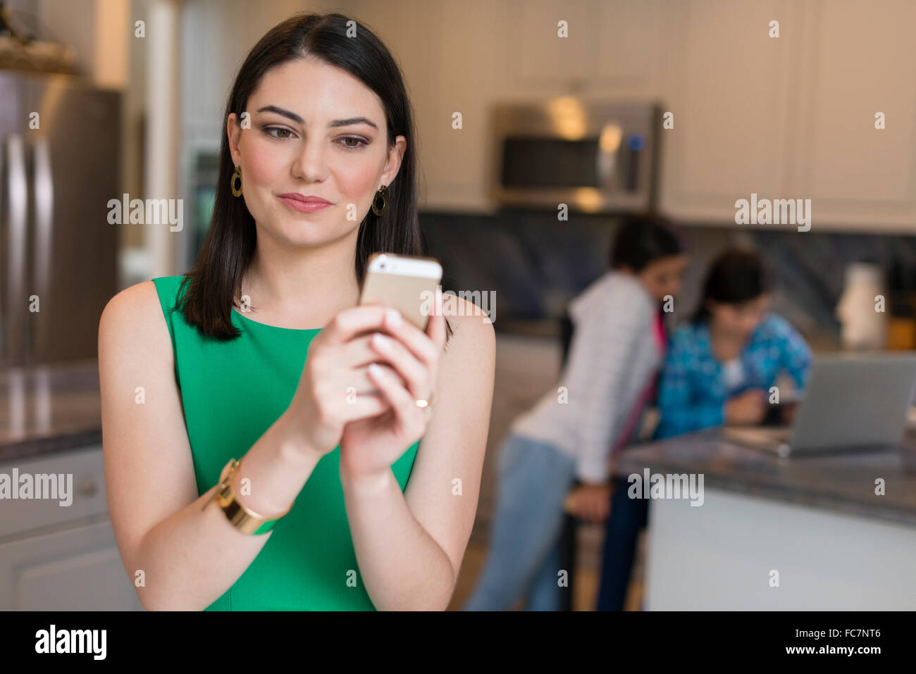 Mother using cell phone in kitchen Stock Photo - Alamy