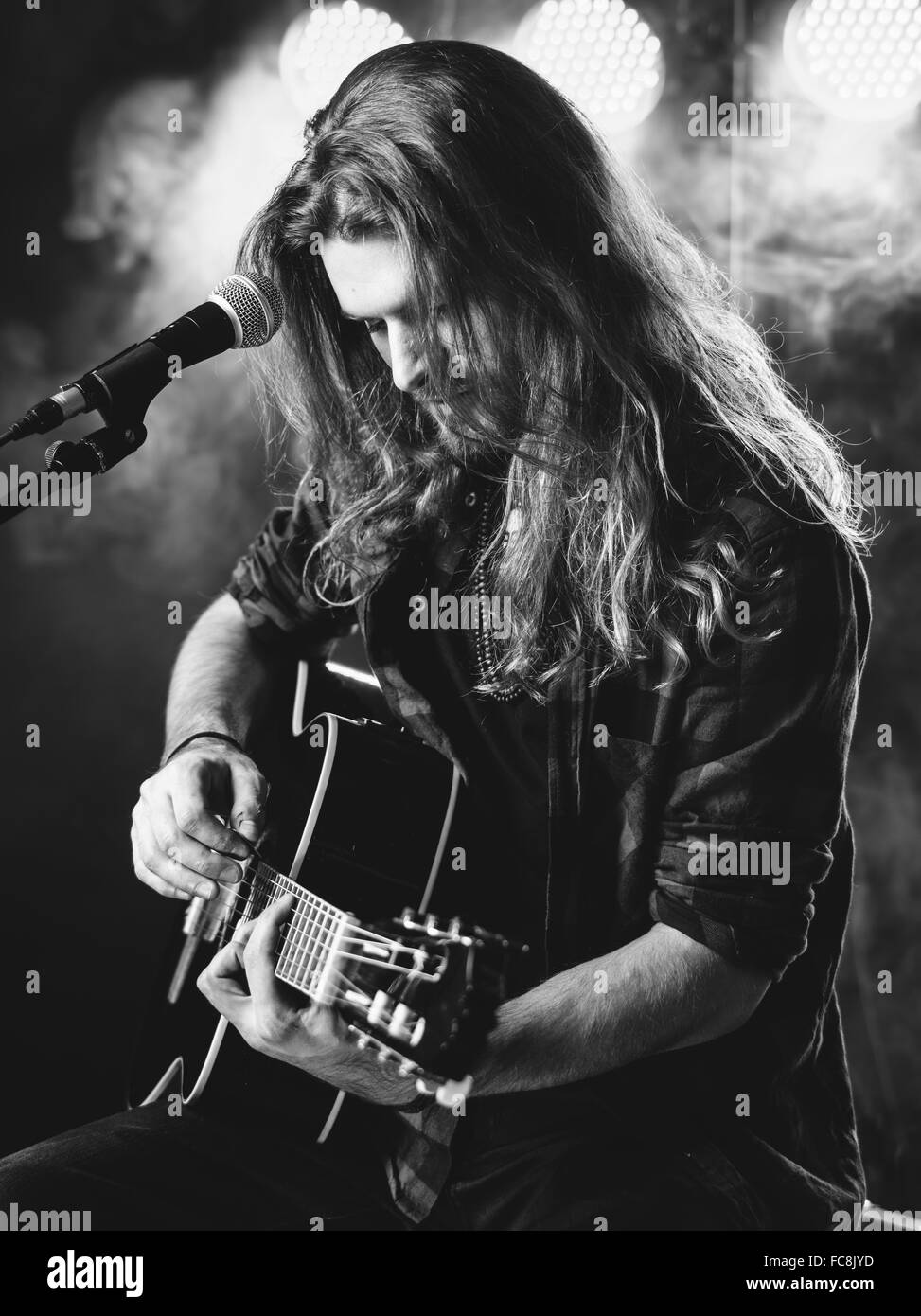 Photo of a young man with long hair and a beard singing and playing an ...