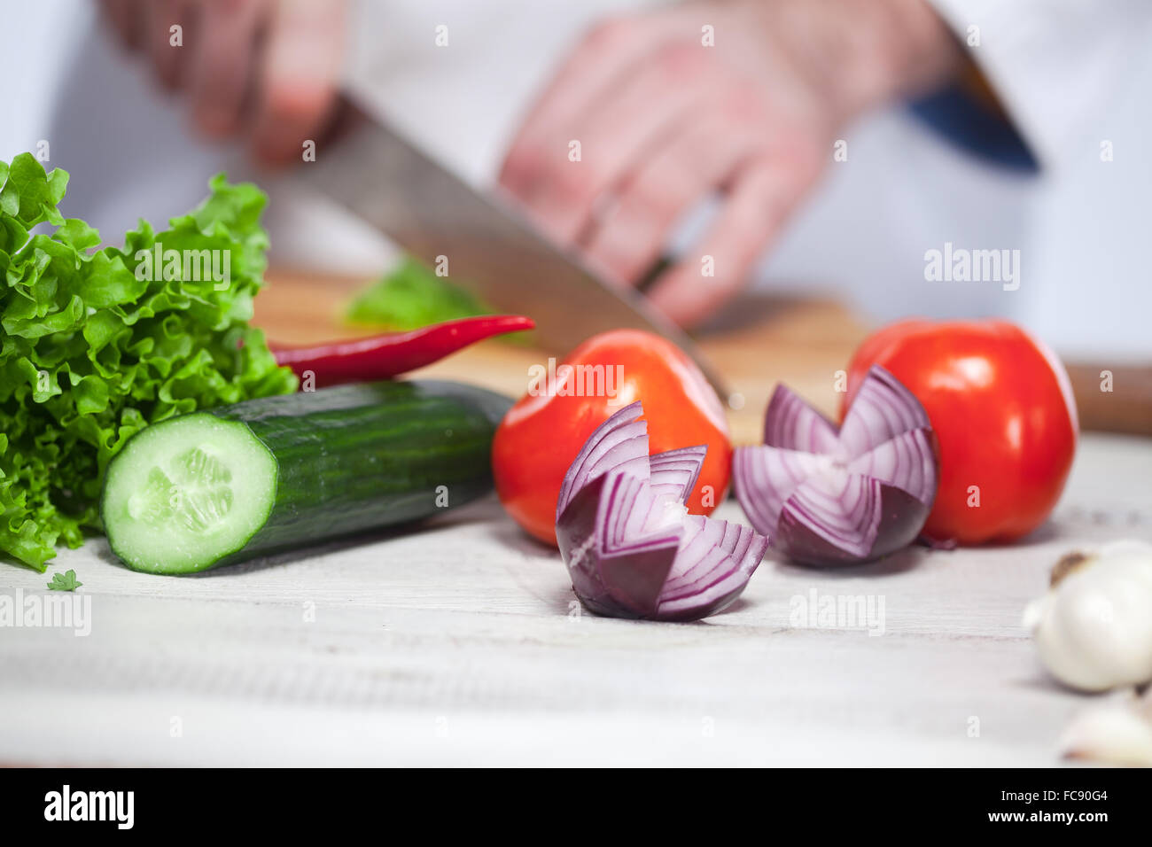 The hands of chef cutting a green lettuce in his kitchen on white ...
